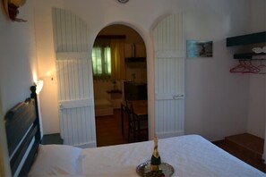 Quarto de hotel com uma cama, uma garrafa de champanhe e uma porta arqueada que dá para uma área de jantar.