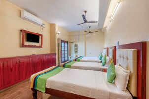 Quarto de hotel com duas camas, televisão, ventoinhas no teto e aparelho de ar condicionado.
