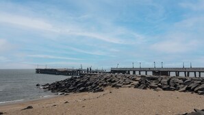 Uma praia com um molhe rochoso e um cais que se estende para a água.