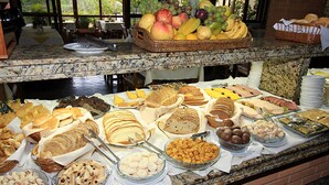 Buffet com diversas opções de comida, incluindo frutas, pães e doces.