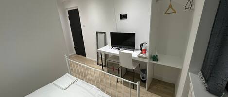 Quarto com cama, escrivaninha com computador, espelho e porta.