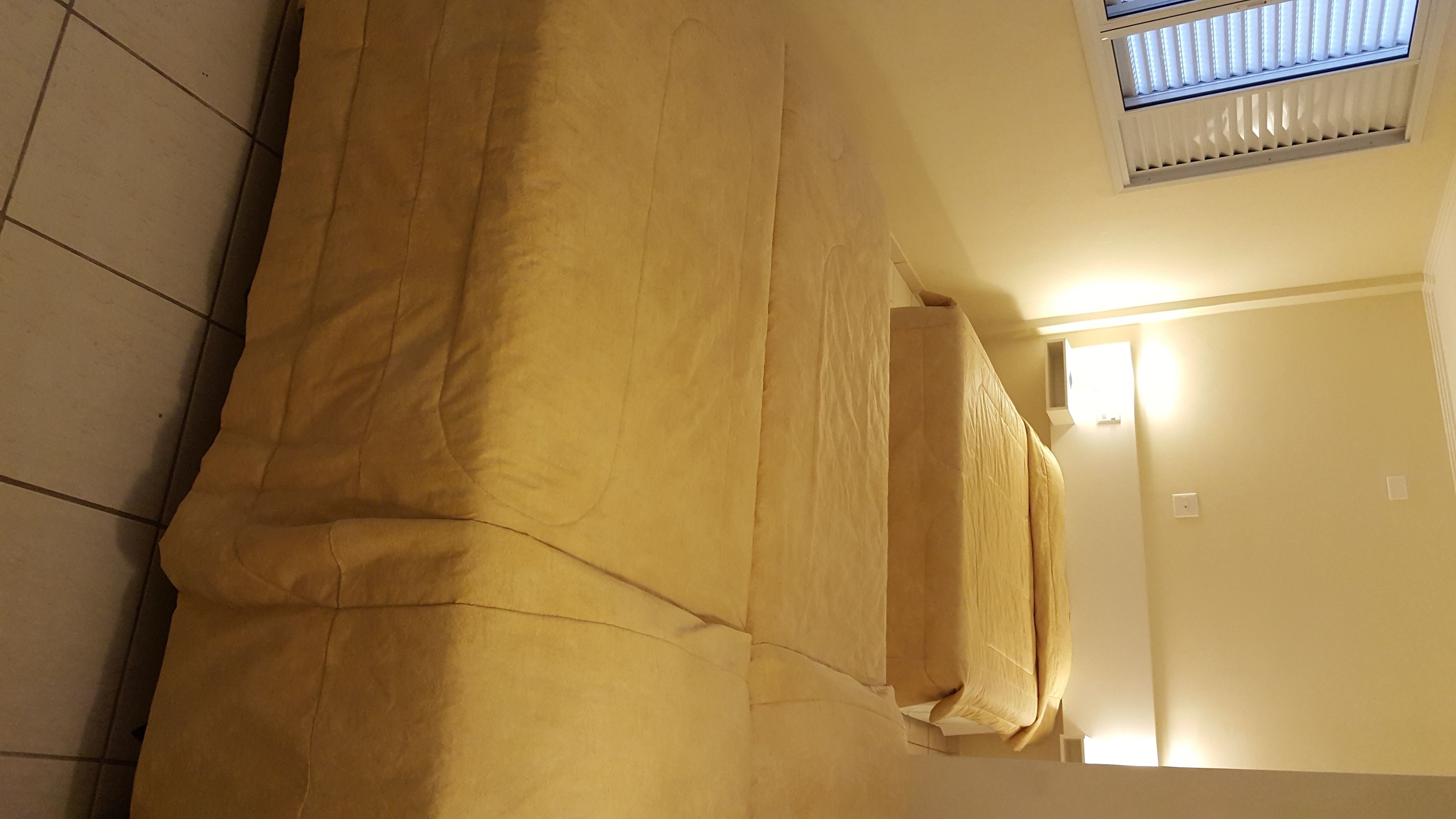 Quarto com cama coberta por lençóis bege, janela com persianas e ar-condicionado fixado na parede.