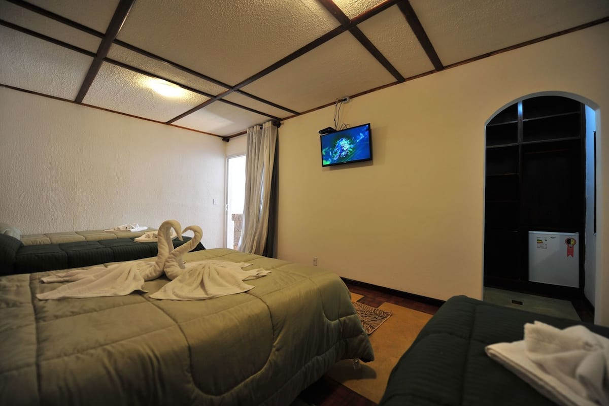 Quarto de hotel com cama, televisão, guarda-roupa e sofá.