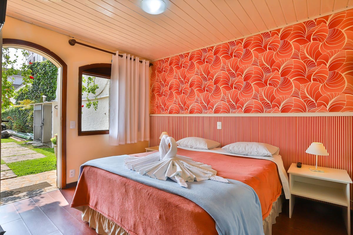 Quarto de hotel com cama, mesa de cabeceira, janela com cortinas e parede estampada.