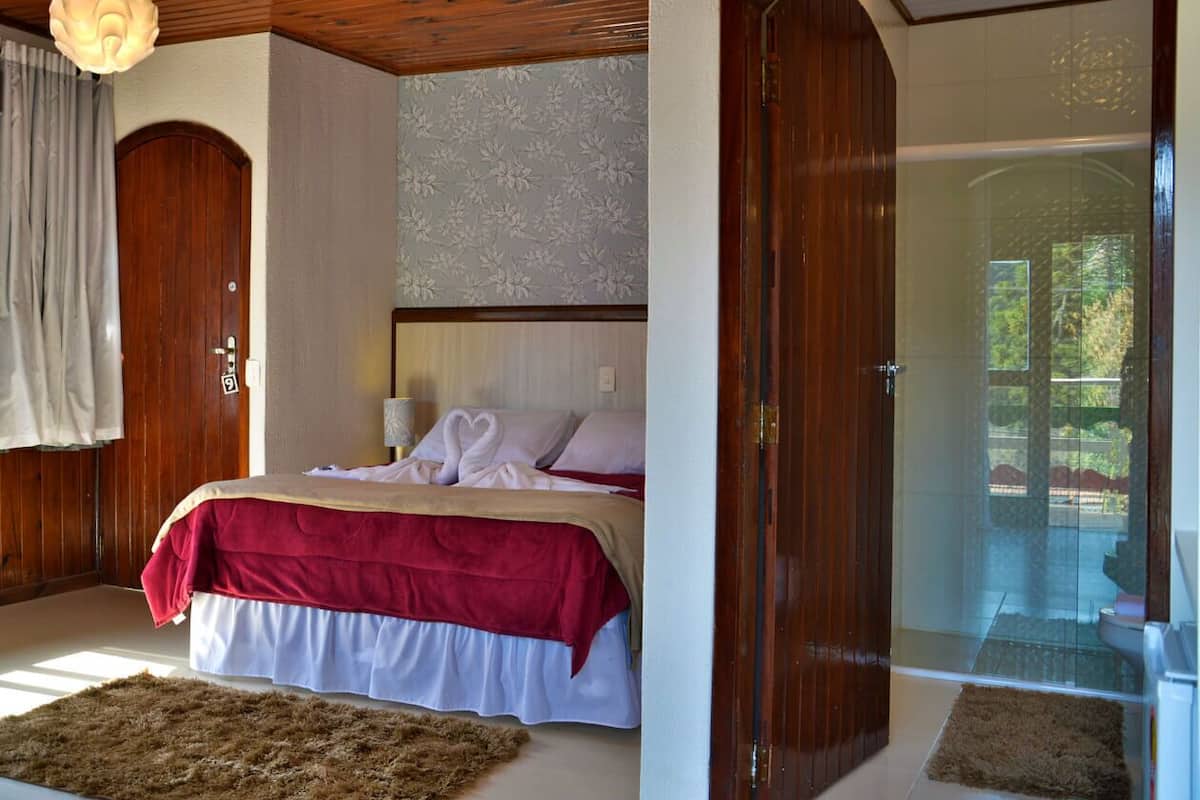 Quarto com cama, porta de madeira e vista para um jardim através de uma porta de vidro.