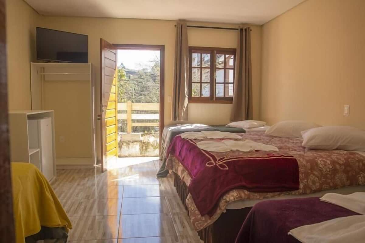 Quarto com cama, televisão, guarda-roupa e janela com cortinas.