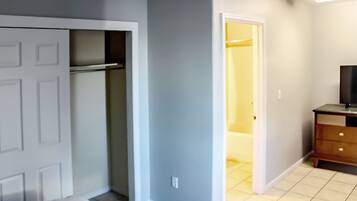 Quarto com porta fechada, armário, cômoda de madeira e televisão.
