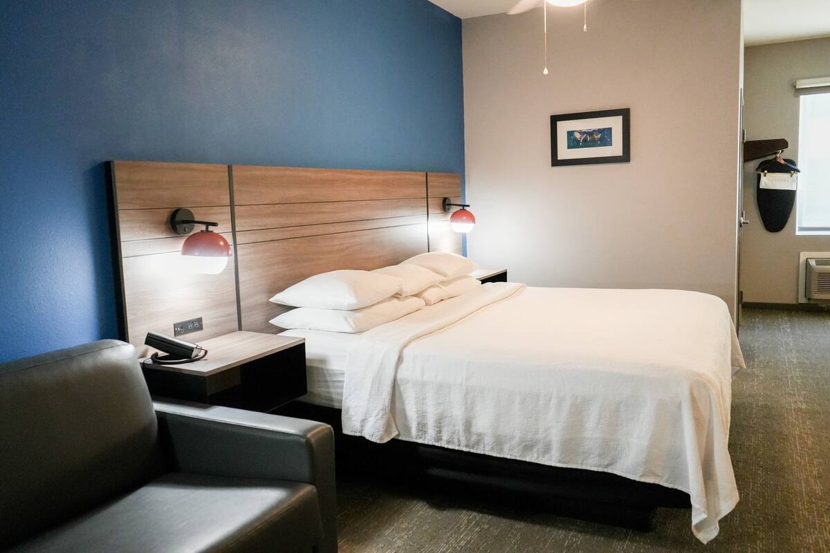 Quarto de hotel com cama, mesas de cabeceira, escrivaninha, cadeira e um quadro pendurado na parede.
