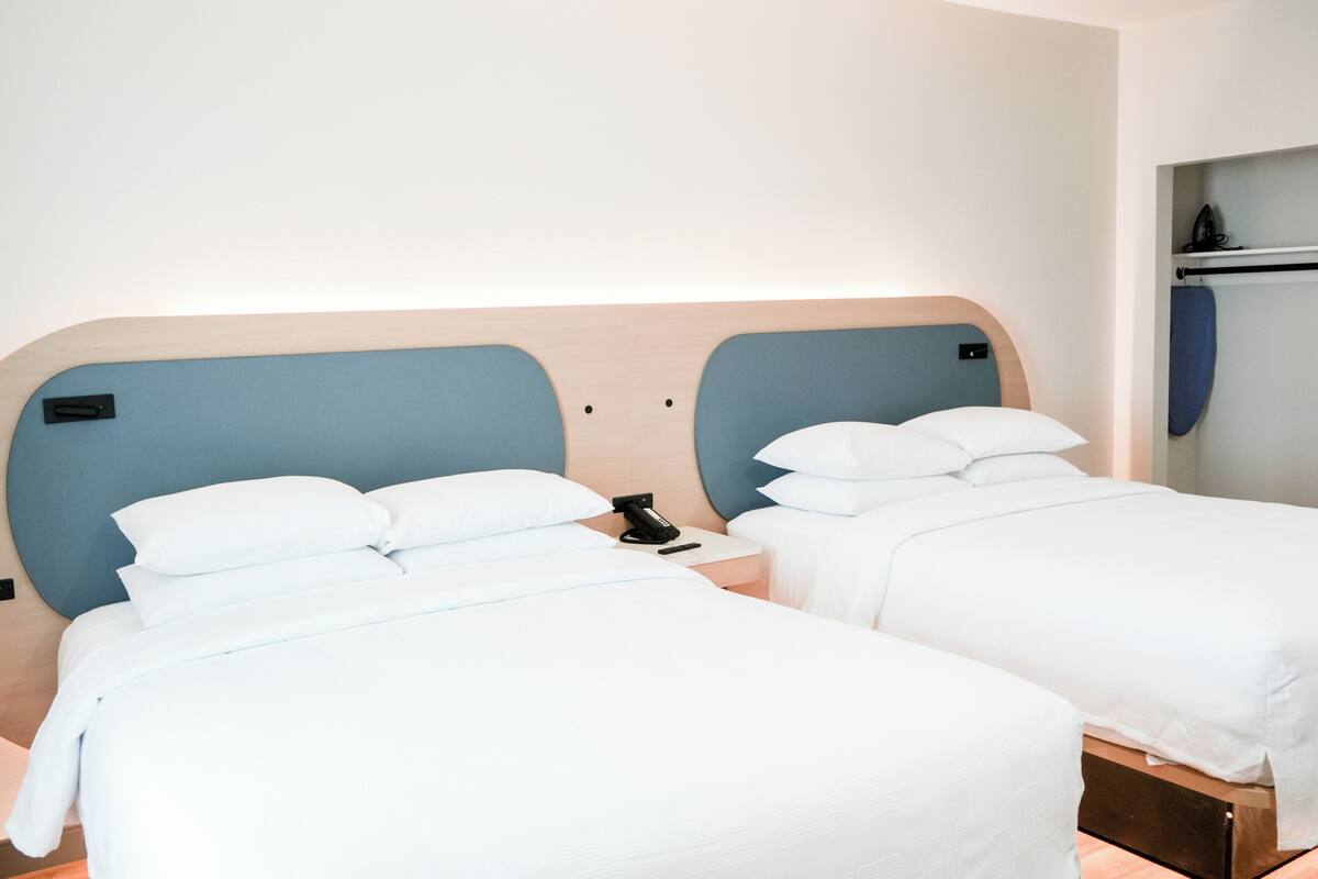 Quarto de hotel com duas camas, cada uma com cabeceira de madeira, mesa de cabeceira e telefone.