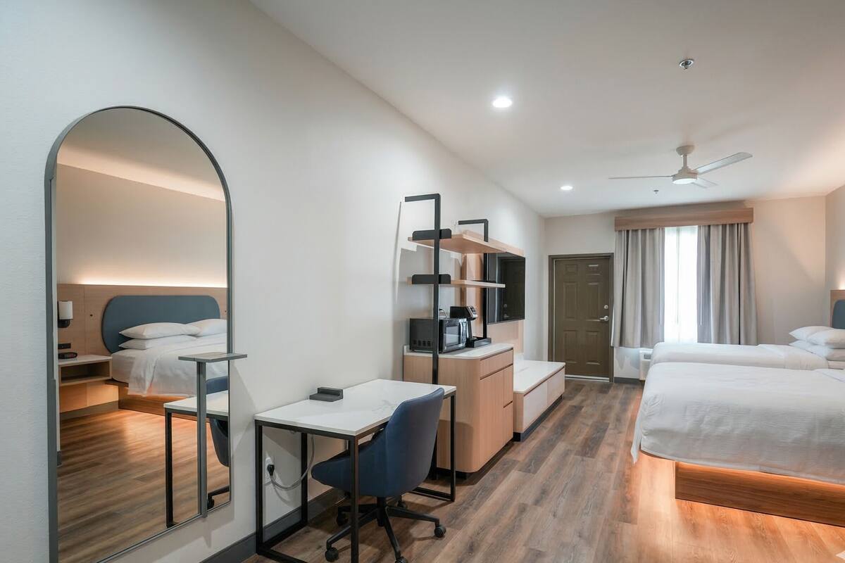Quarto de hotel com cama, escrivaninha, cadeira e espelho.
