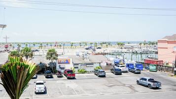 Um estacionamento com vários veículos, um edifício com uma placa e uma praia ao fundo.