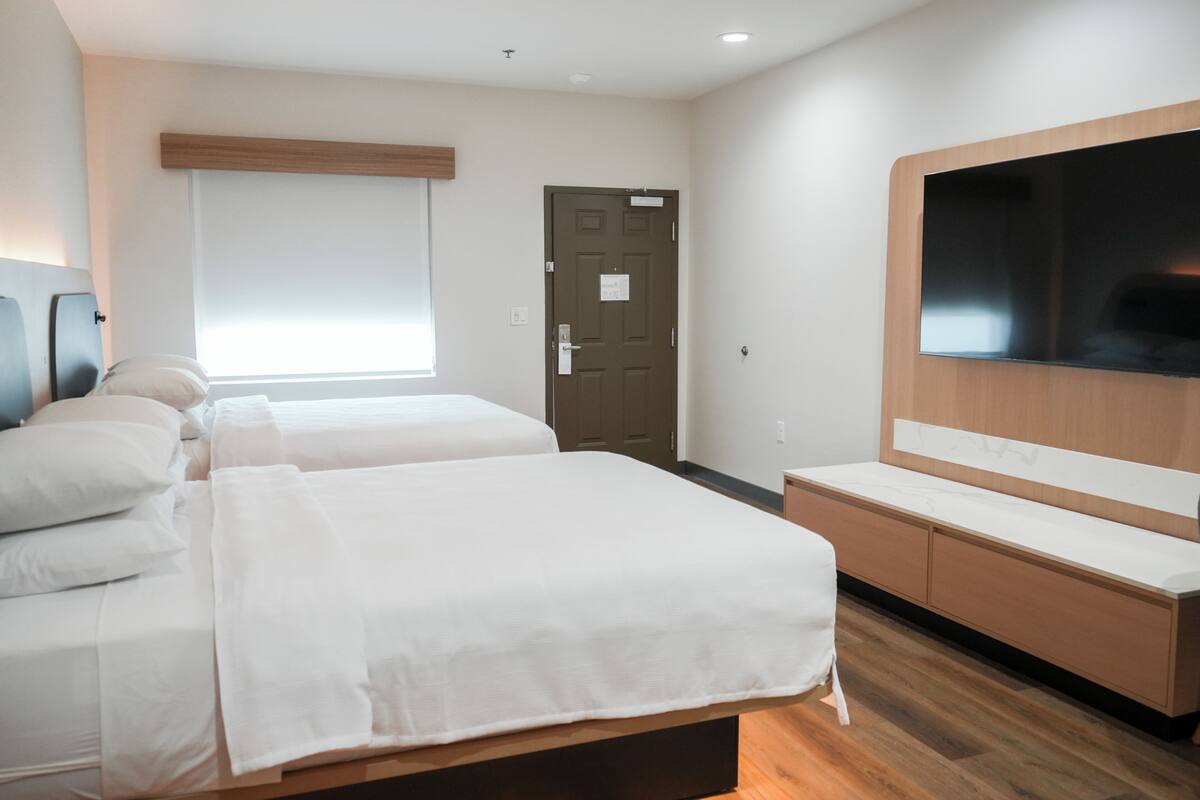 Quarto de hotel com duas camas, televisão, armário de madeira e uma porta.