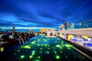 Piscina infinita no terraço com vista para a cidade, espreguiçadeiras e guarda-corpo de vidro.
