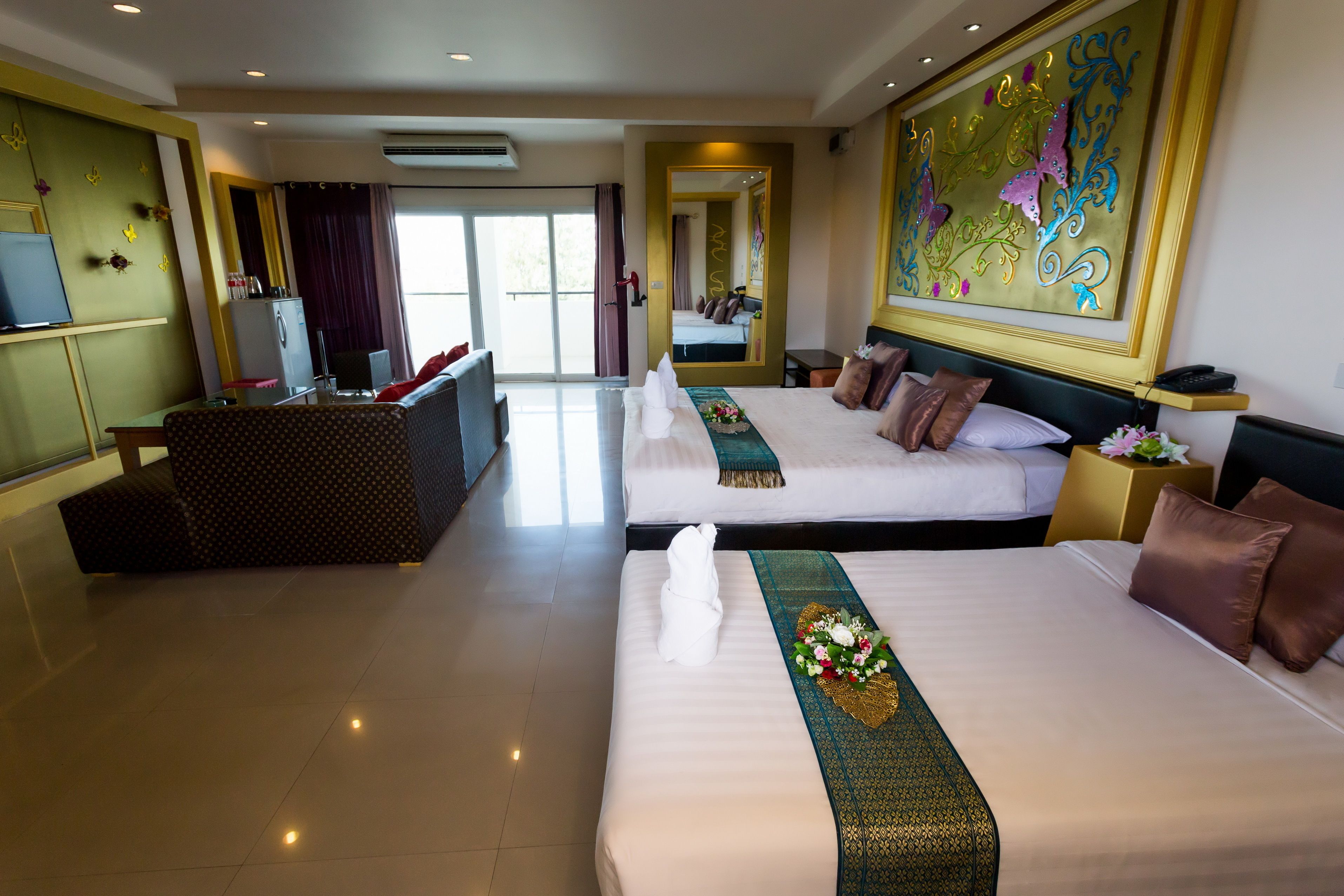 Quarto de hotel com duas camas, um espaço de estar, uma TV e um painel decorativo grande na parede.