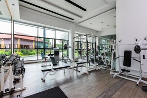 Uma academia moderna com diversos equipamentos de musculação, amplas janelas e vista para o verde lá fora.