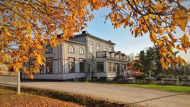 Um edifício de dois andares com uma varanda, rodeado por folhas de outono.