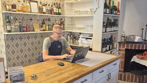 Uma área de bar com prateleiras de garrafas de bebidas, copos e um laptop no balcão.