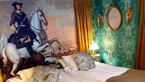 Quarto com uma cama grande, duas almofadas, mesa de cabeceira com abajur, espelho e pintura na parede de um cavaleiro e seu cavalo.