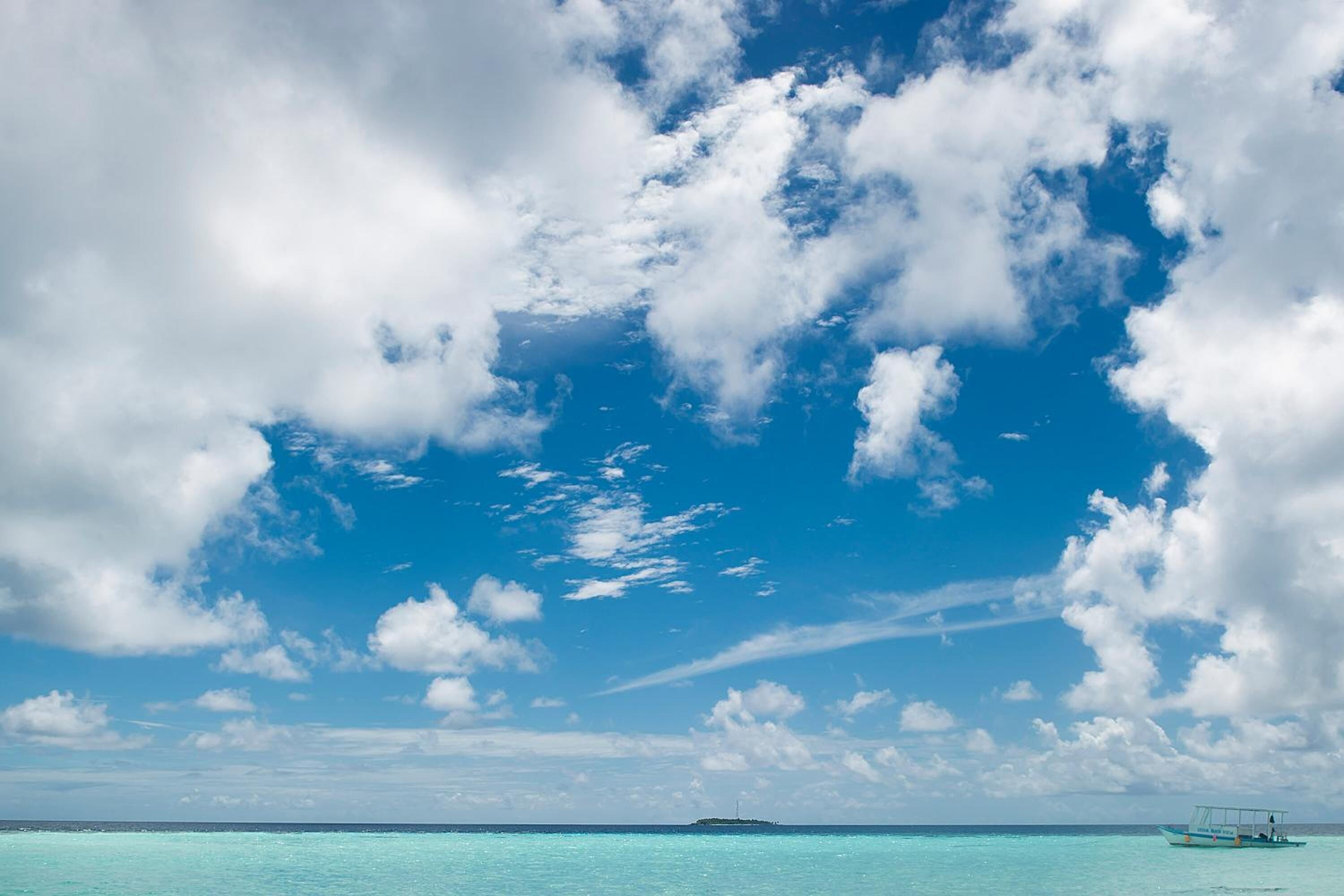 Céu azul límpido com algumas nuvens sobre um mar calmo.