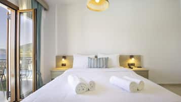 Quarto de hotel com uma cama grande, duas mesas de cabeceira com abajures, vista através de uma porta de correr para uma área externa, e um lustre.