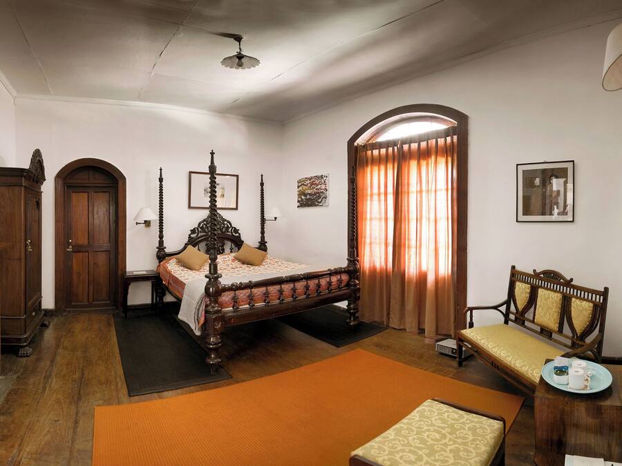 Um quarto tradicional com uma cama de dossel, um guarda-roupa de madeira, um espaço de estar com um banco e uma mesa de jantar com cadeiras.