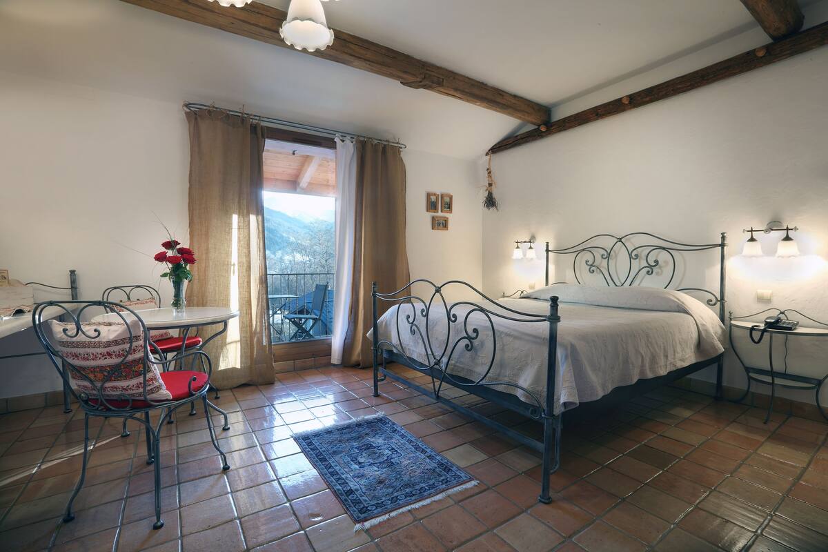 Quarto com cama, cadeira, mesa e vista para o exterior.