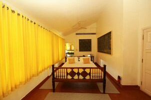 Quarto com cama de madeira, cortinas amarelas, ventoinha no teto e mesa de cabeceira com abajur.