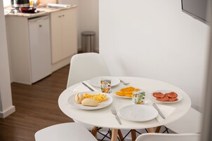 Mesa de jantar com pratos de comida, incluindo ovos mexidos, fatias de laranja e tomates fatiados. Há dois pacotes de suco de laranja e um garfo na mesa.