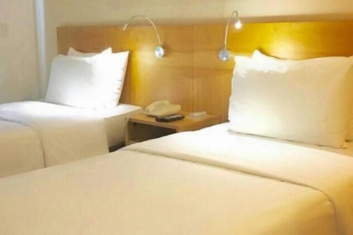 Quarto de hotel com duas camas, uma mesa de cabeceira com abajur e um telefone.
