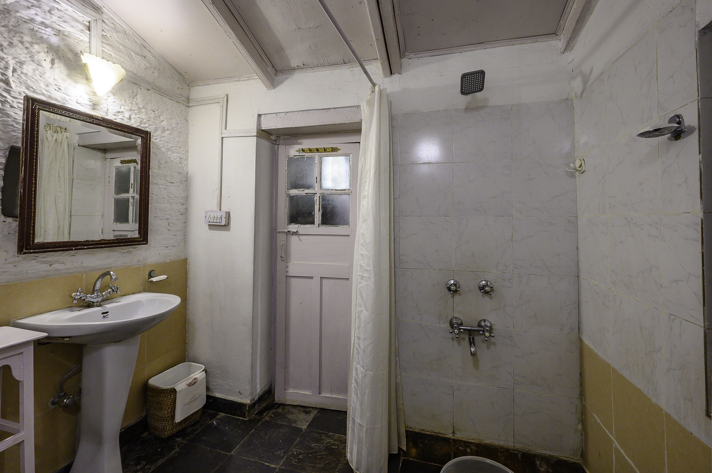 Uma casa de banho com lavatório, espelho, chuveiro e uma porta que dá para outro espaço.