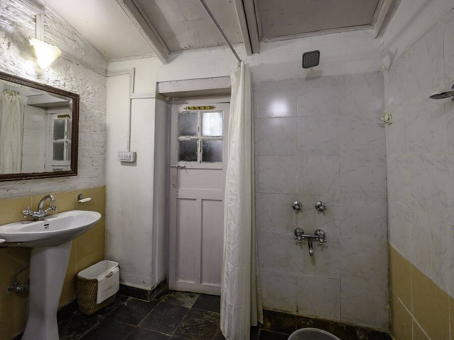 Uma casa de banho com lavatório, espelho, chuveiro e uma porta que dá para outro espaço.