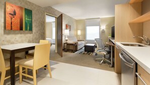 Quarto de hotel moderno com área de refeições, sofá, escrivaninha e cozinha.