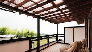 Um deck de madeira com pérgola, duas cadeiras estofadas e vista para o verde.