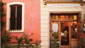 A Neemrana Shop com fachada de madeira, grandes janelas e plantas em vasos do lado de fora.