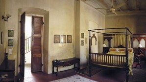 Uma cama tradicional com dossel e cortinas, um banco de madeira e quadros na parede.