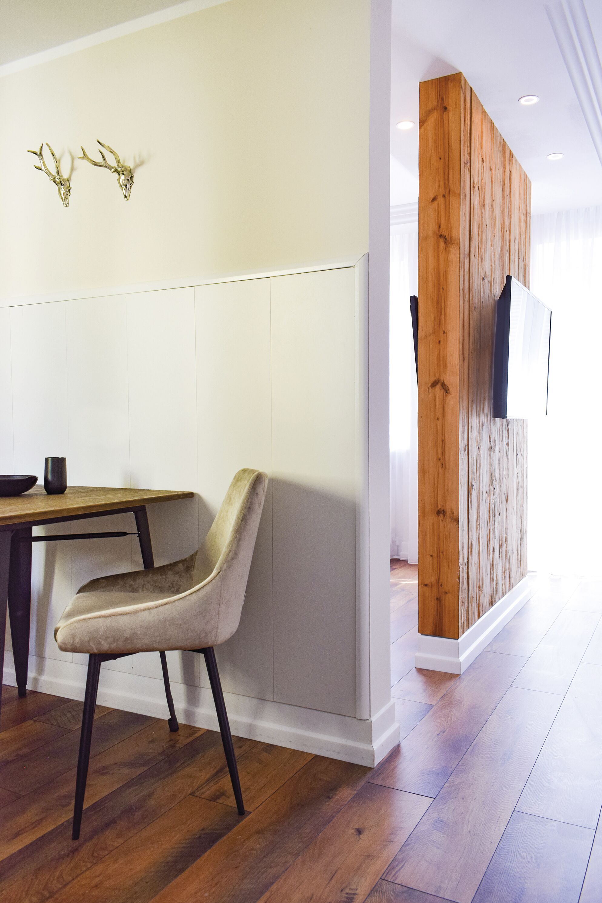 Uma sala de jantar moderna com uma mesa de madeira, cadeiras estofadas e uma televisão fixada na parede.