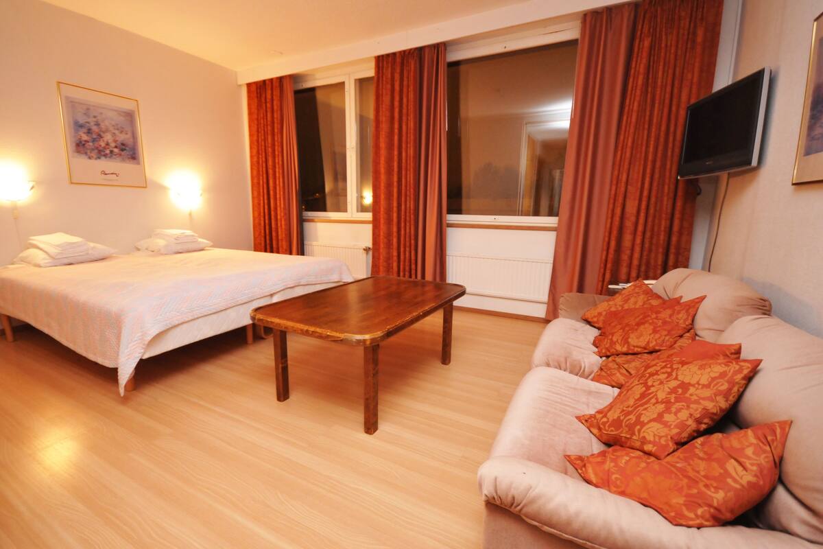 Quarto de hotel com cama, mesa de madeira, sofá e televisão na parede.