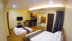 Quarto de hotel com duas camas, televisão, cozinha compacta e espelho.
