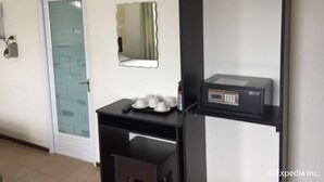 Quarto de hotel com escrivaninha preta, micro-ondas, armário pequeno, porta de vidro e espelho na parede.