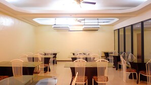 Sala de conferências com mesas, cadeiras, ventiladores de teto e aparelhos de ar condicionado.