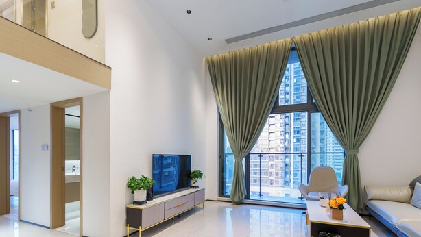 Uma sala de estar moderna com uma TV de tela plana, um sofá, uma mesa de centro e vista para um horizonte urbano através de grandes janelas.