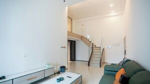 Uma sala de estar moderna com um sofá verde, uma mesa de centro branca e uma escada que leva a outro andar.