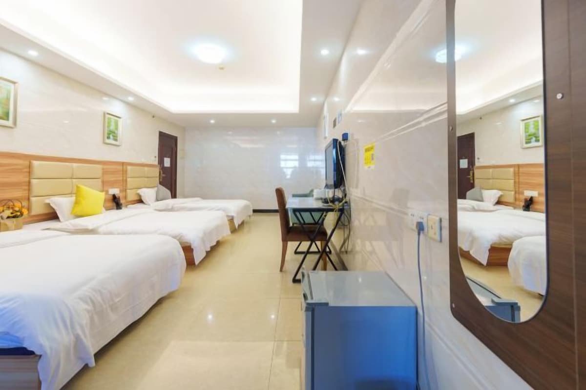 Quarto de hotel com quatro camas de solteiro, uma escrivaninha e um espelho.
