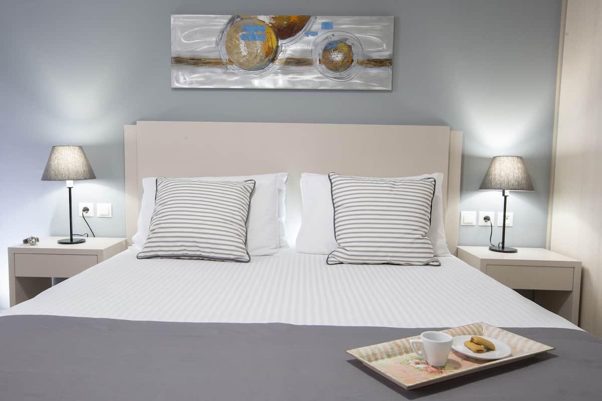 Uma cama bem arrumada com almofadas listradas, um tabuleiro com uma chávena e uma banana, e um quadro em cima.