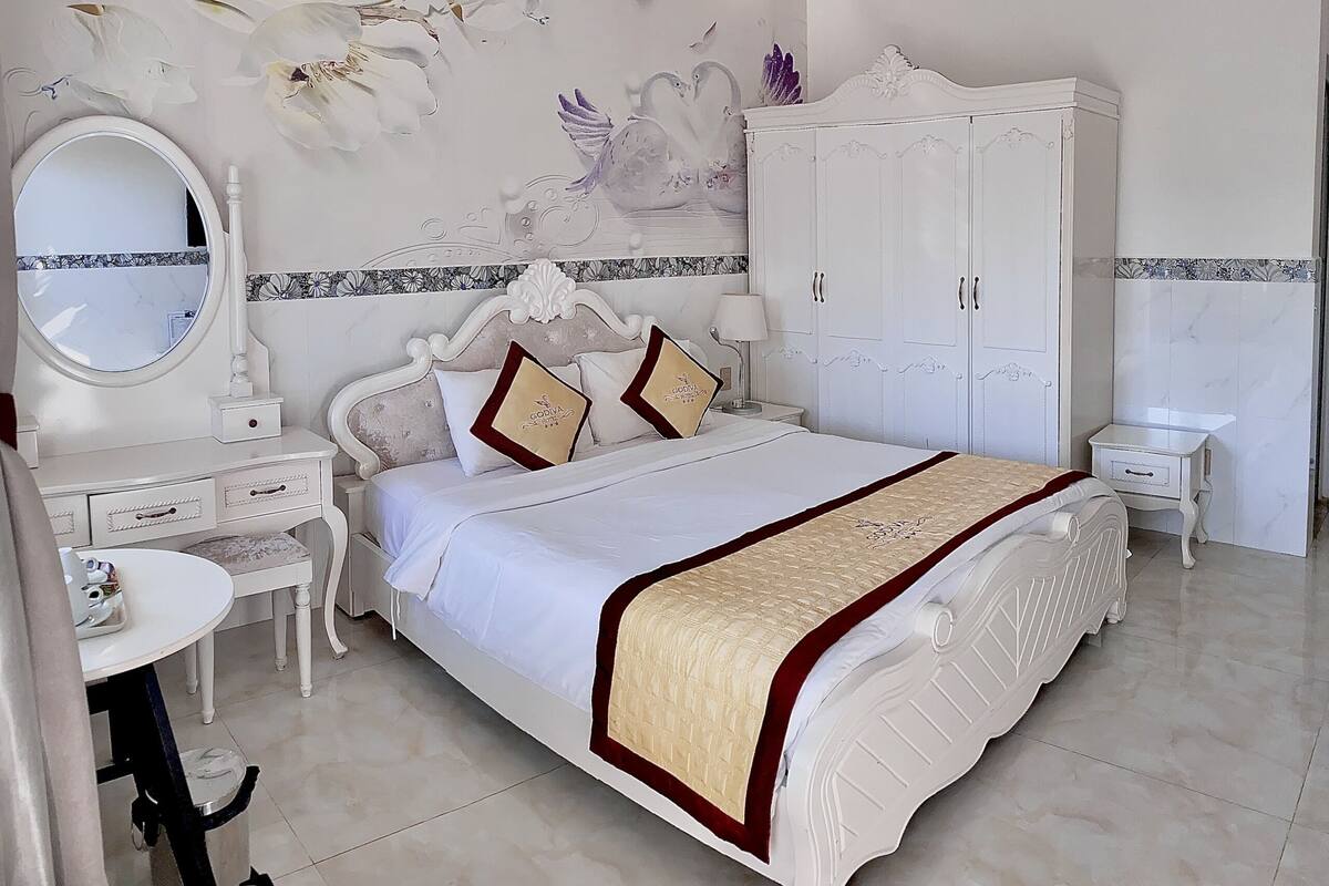 Quarto com uma cama grande, um guarda-roupa, uma toucador e um espelho.