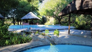 Uma área de piscina com várias piscinas, estruturas com telhados de palha e vegetação ao redor.