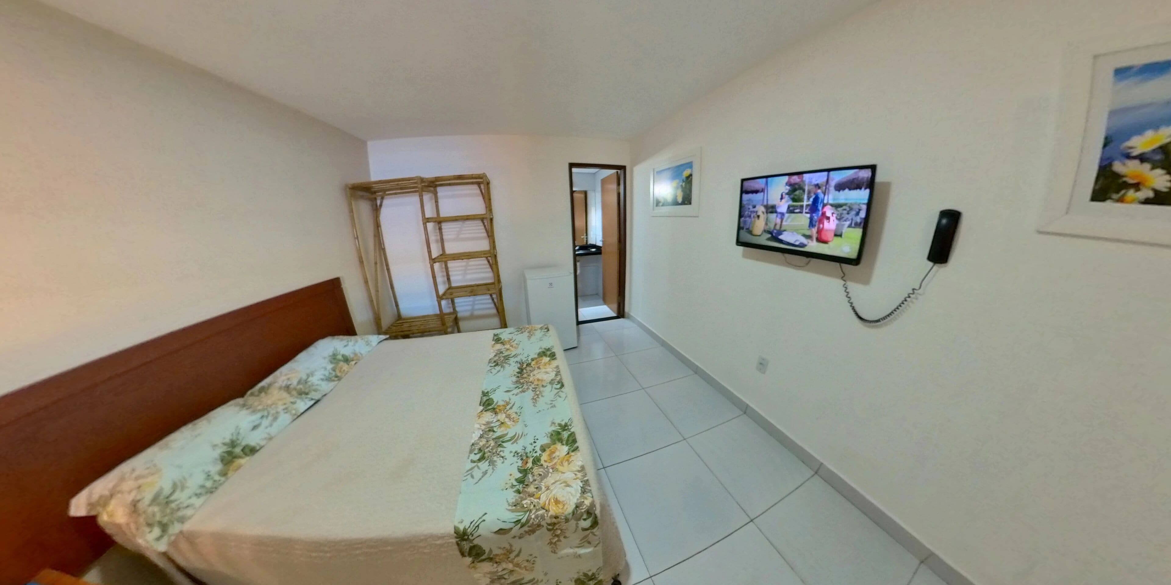 Quarto com cama, televisão na parede e porta que dá para outro cômodo.