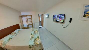 Quarto com cama, televisão na parede e porta que dá para outro cômodo.
