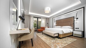 Quarto moderno com uma cama grande, uma escrivaninha com cadeira, um sofá e uma janela ampla.