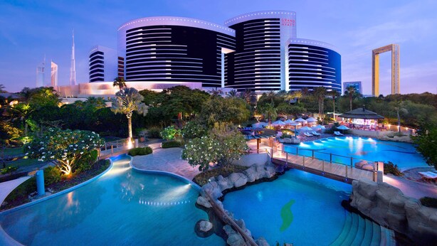 Um hotel com uma ampla área de piscina ao ar livre, várias piscinas e fachada bem iluminada.